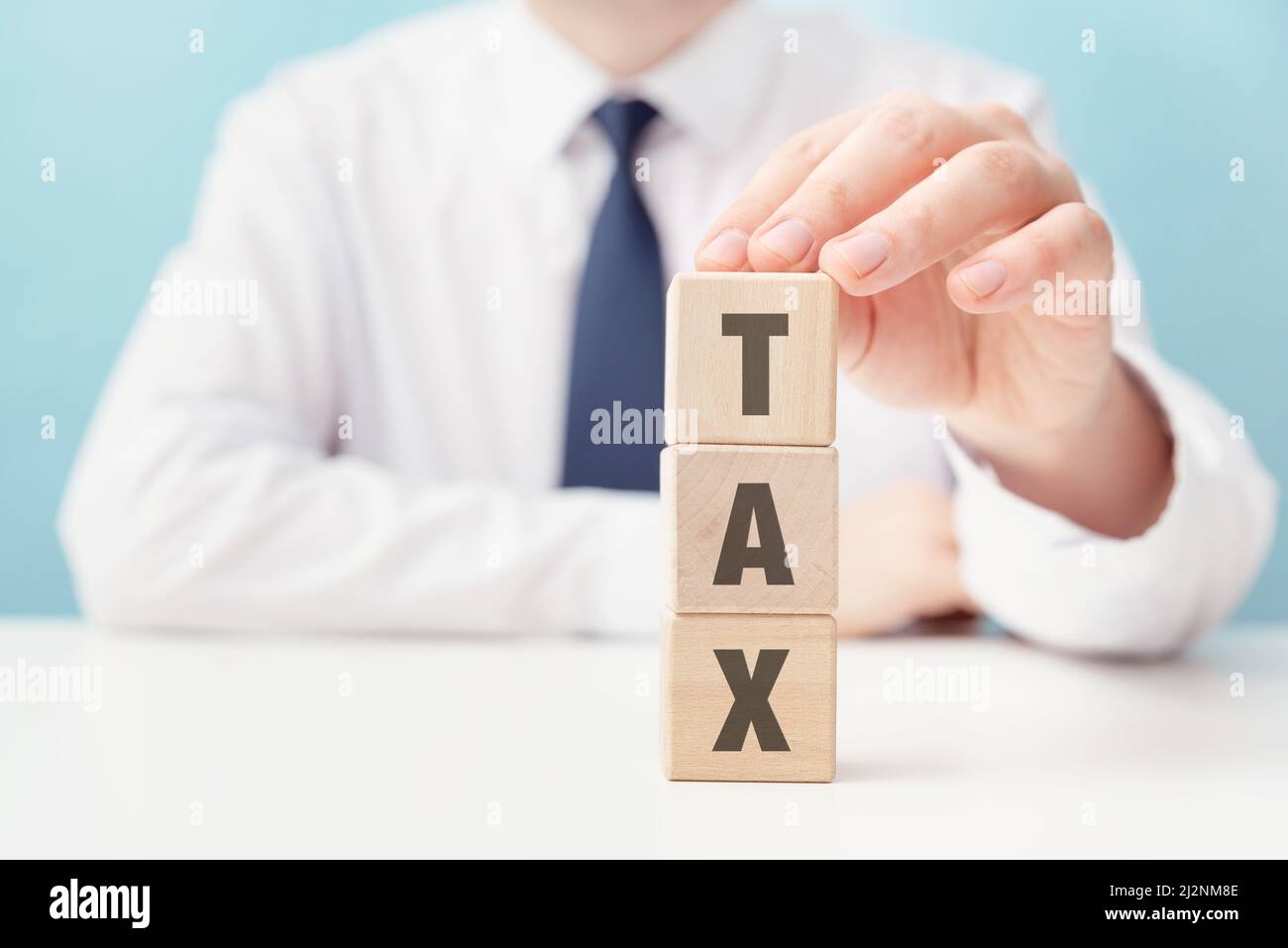 Concept of tax. Businessman builds tower with tax word from wooden ...