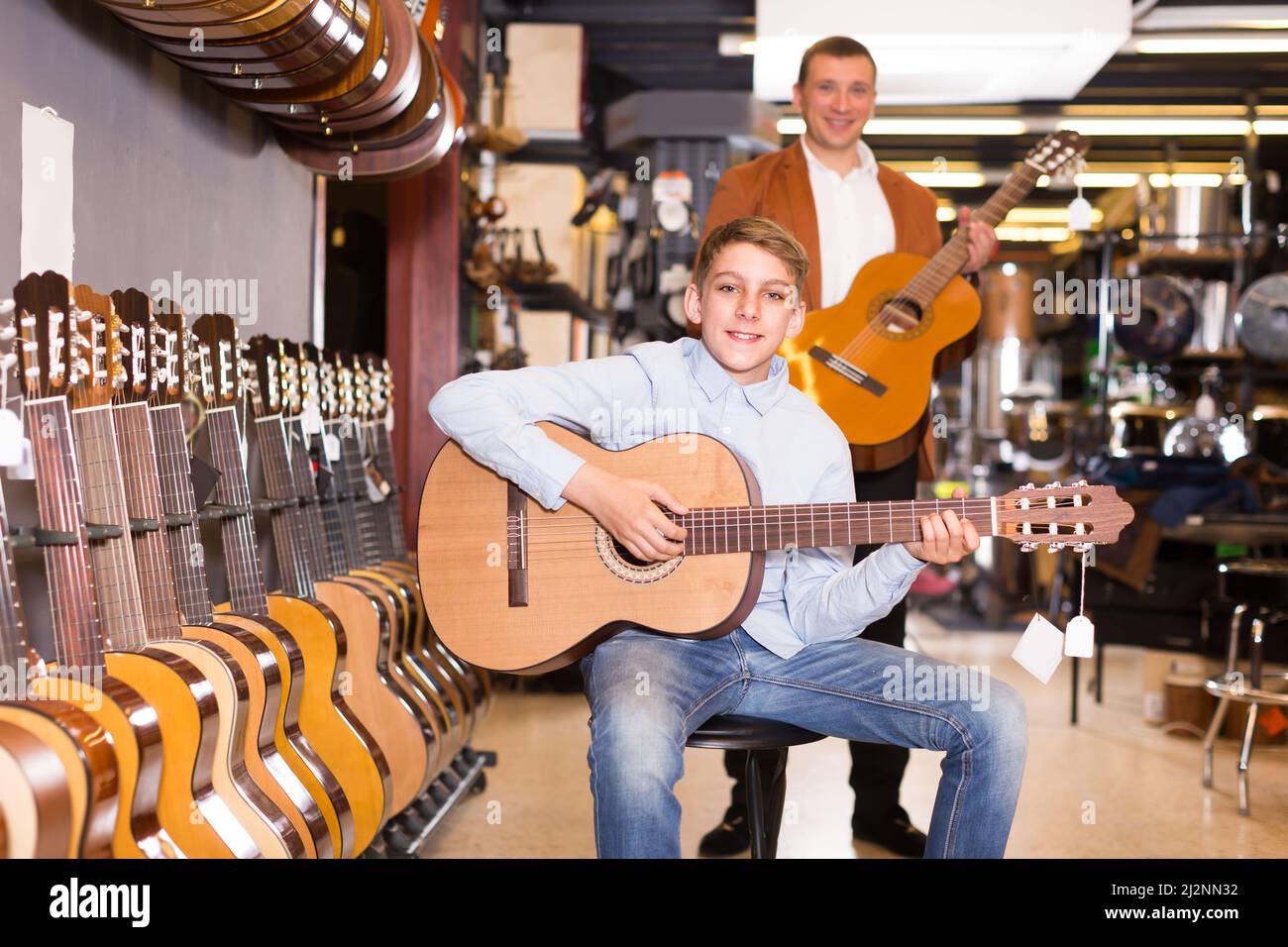Cheerful seller showing guitar to boy client Stock Photo - Alamy