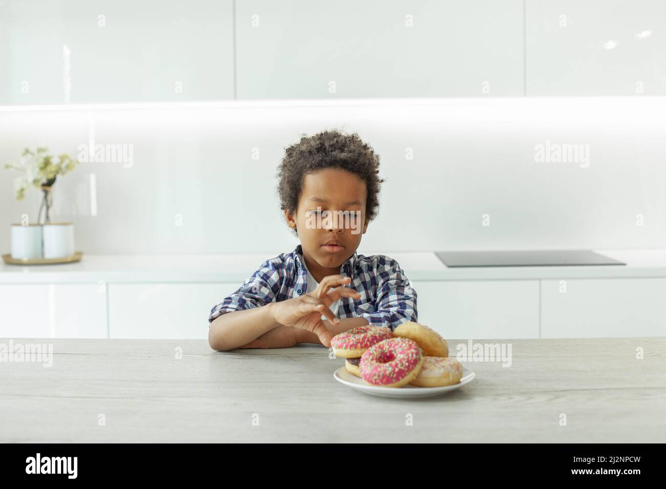 Cute kid boy with black hair eating donuts in white kitchen Stock Photo ...