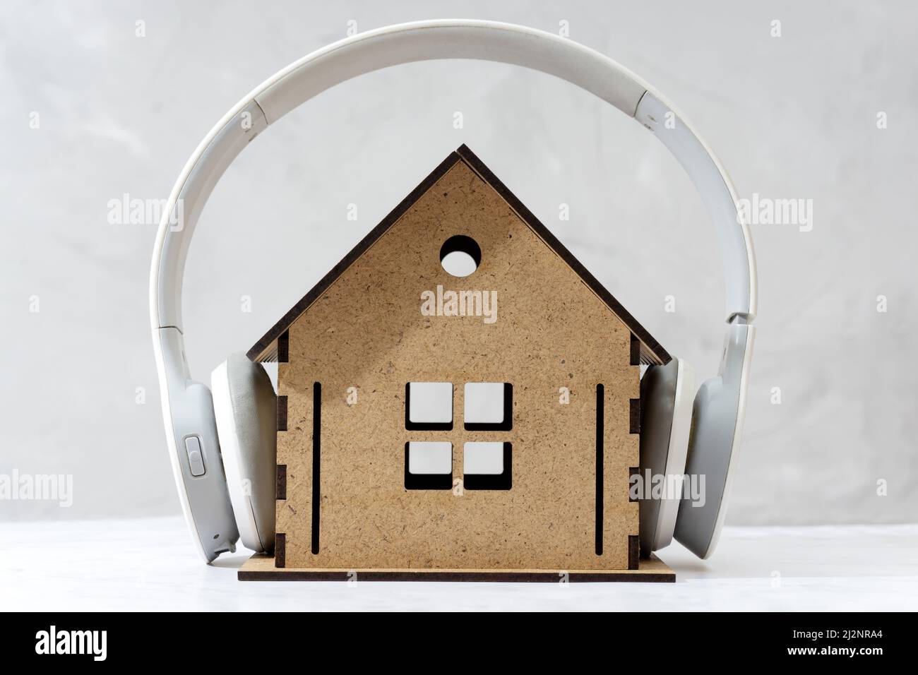 Close-up of white wireless headphones on a small wooden house against a ...
