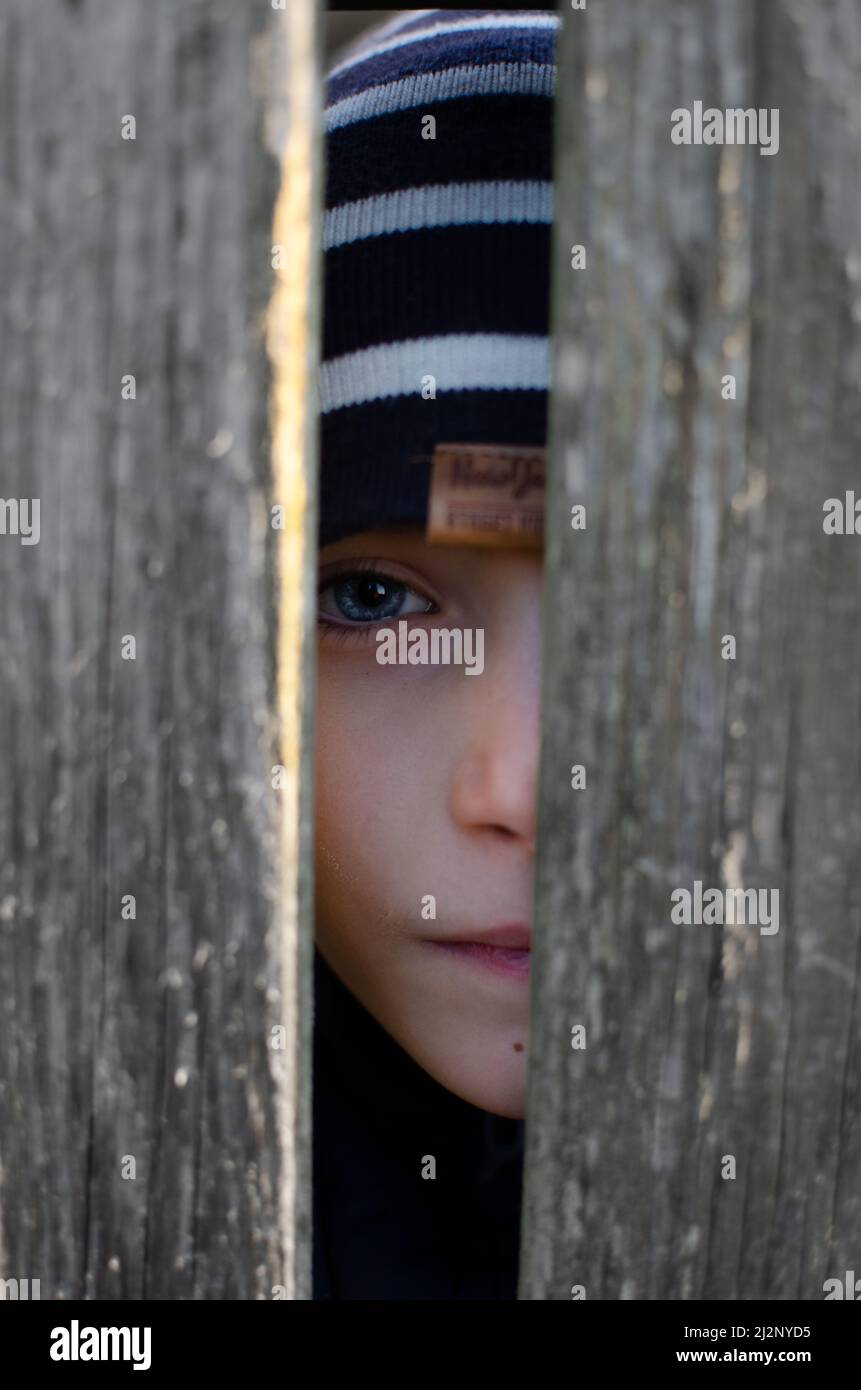 Boy looking through a gap in the fence Stock Photo - Alamy