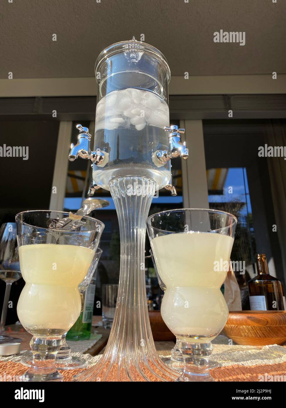 Absinth fountain with water and ice cube and four glasses and spoon ...