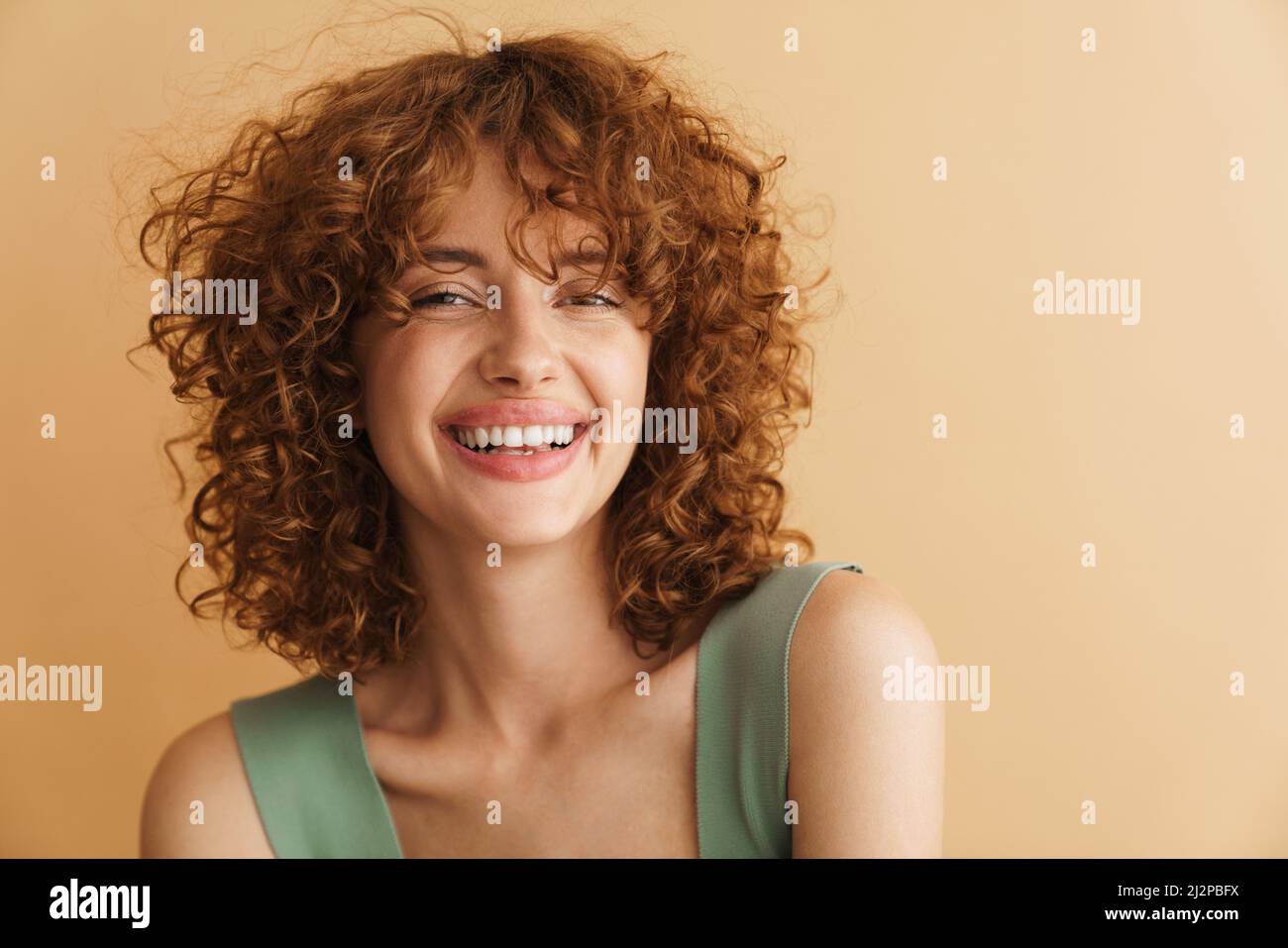 Young ginger woman laughing while posing at camera isolated over beige ...