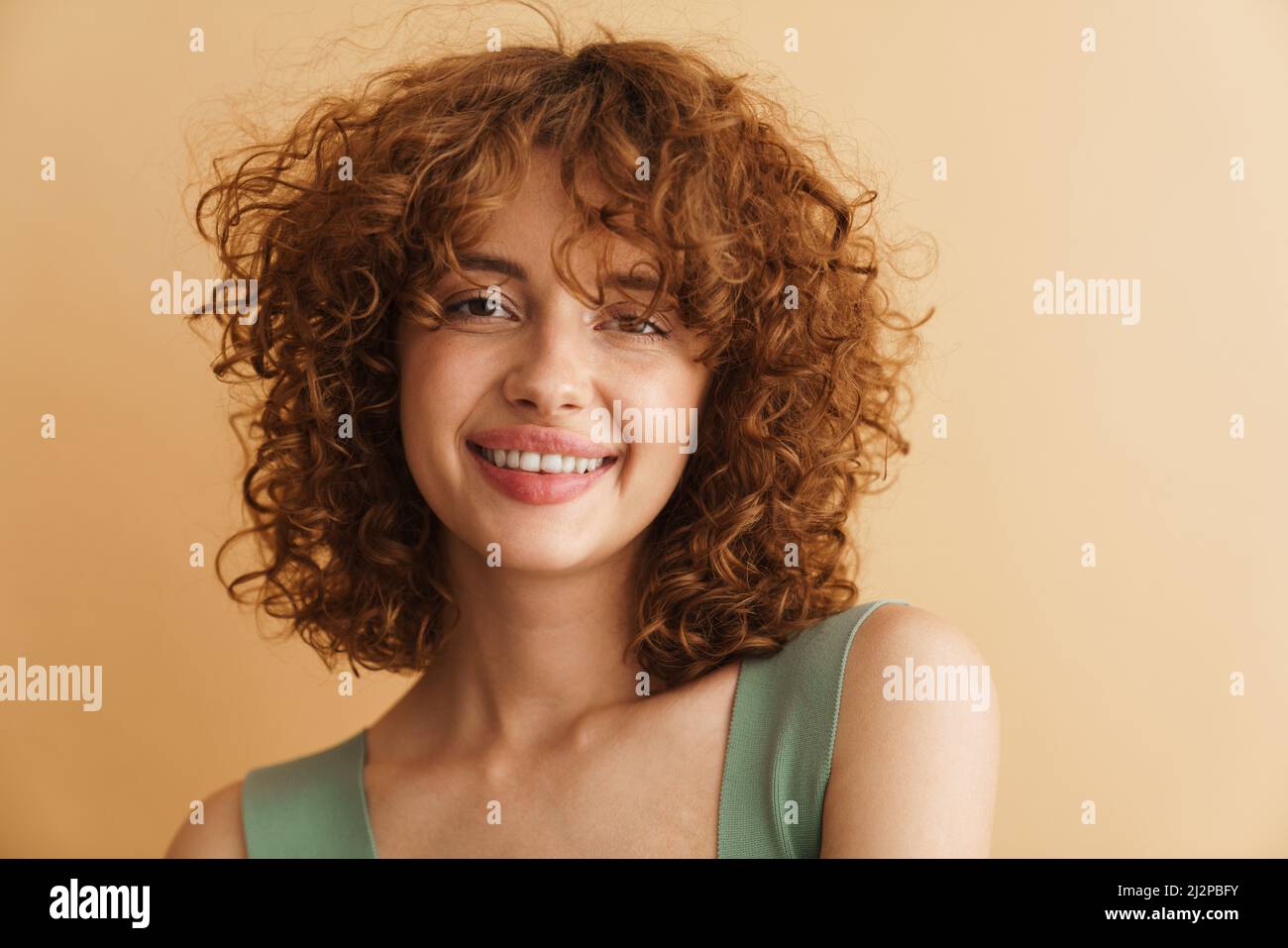 Young ginger woman laughing while posing at camera isolated over beige ...