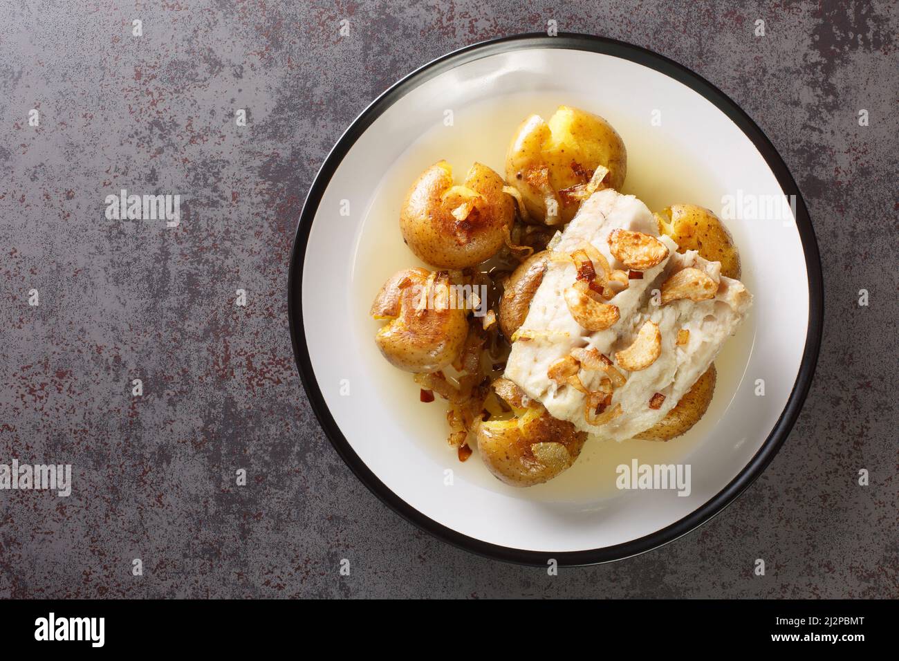 Cod fillet baked in olive oil with garlic served with potatoes close-up ...