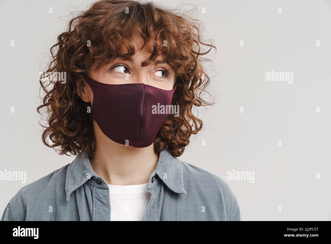 Young ginger pleased woman in face mask looking at camera isolated over ...