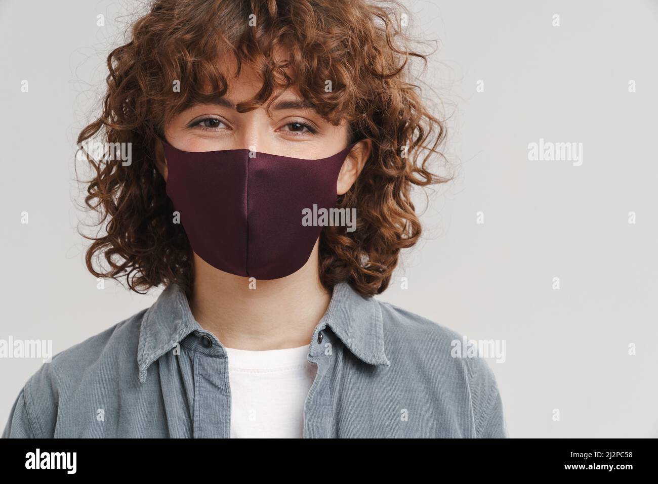 Young ginger pleased woman in face mask looking at camera isolated over ...