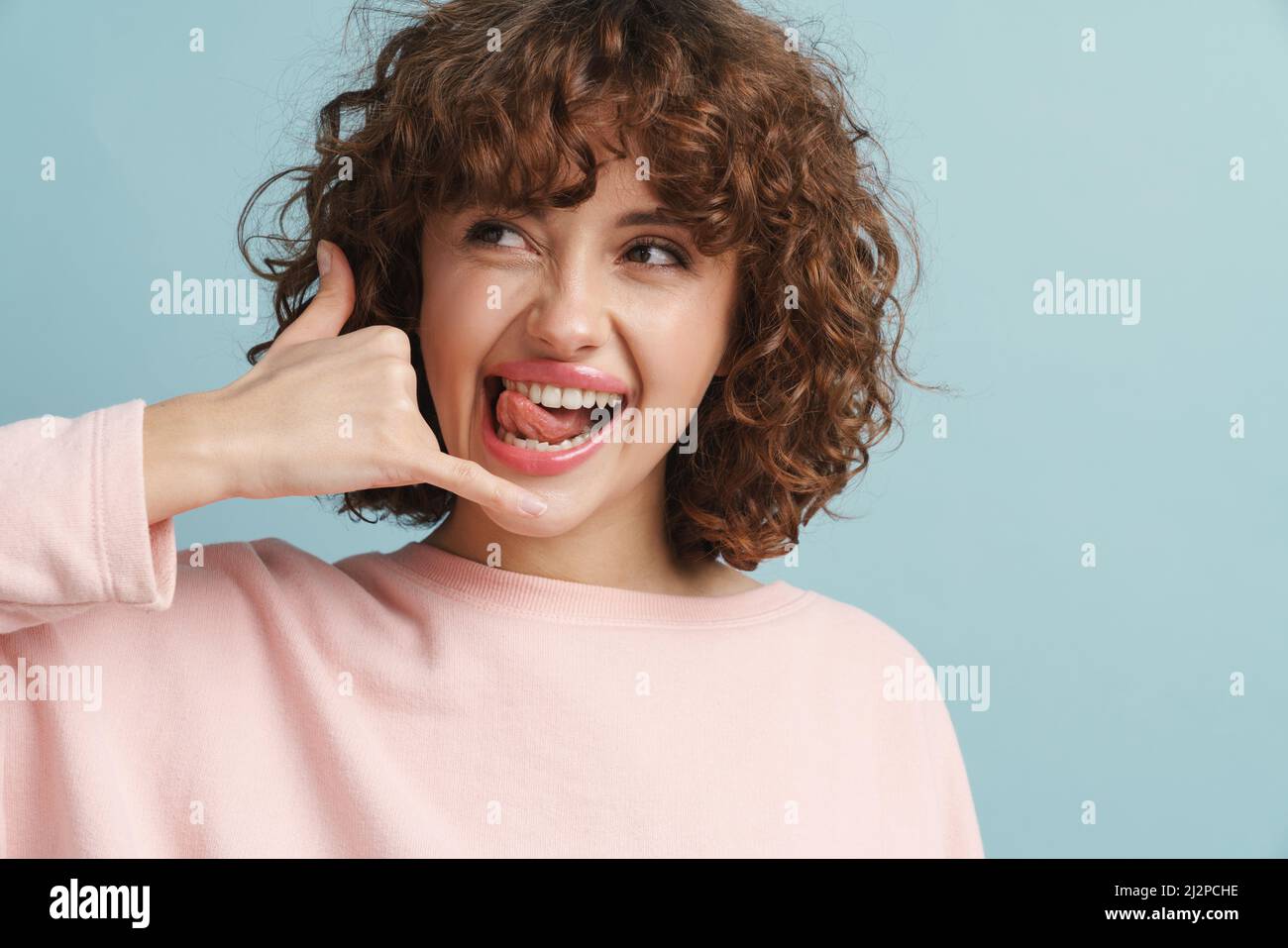 Young happy woman showing her tongue and showing handset gesture ...