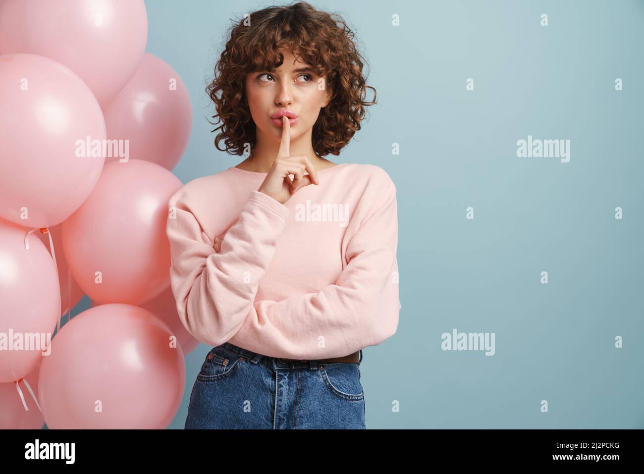 Young woman showing silence gesture while posing with pink balloons ...