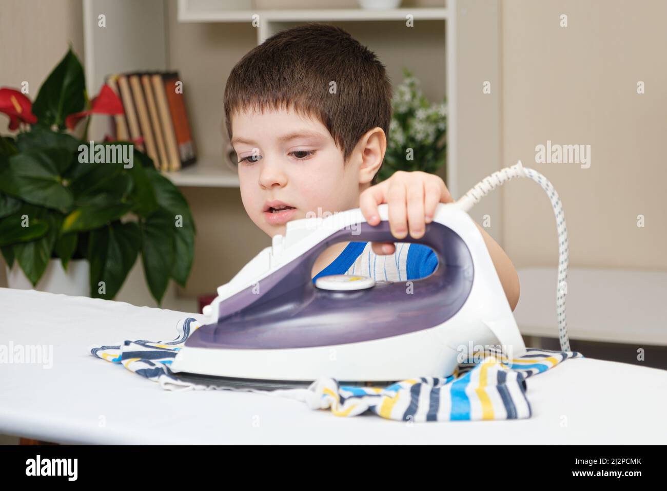 A boy of 4 years learns to hold an iron, iron clothes on an ironing ...