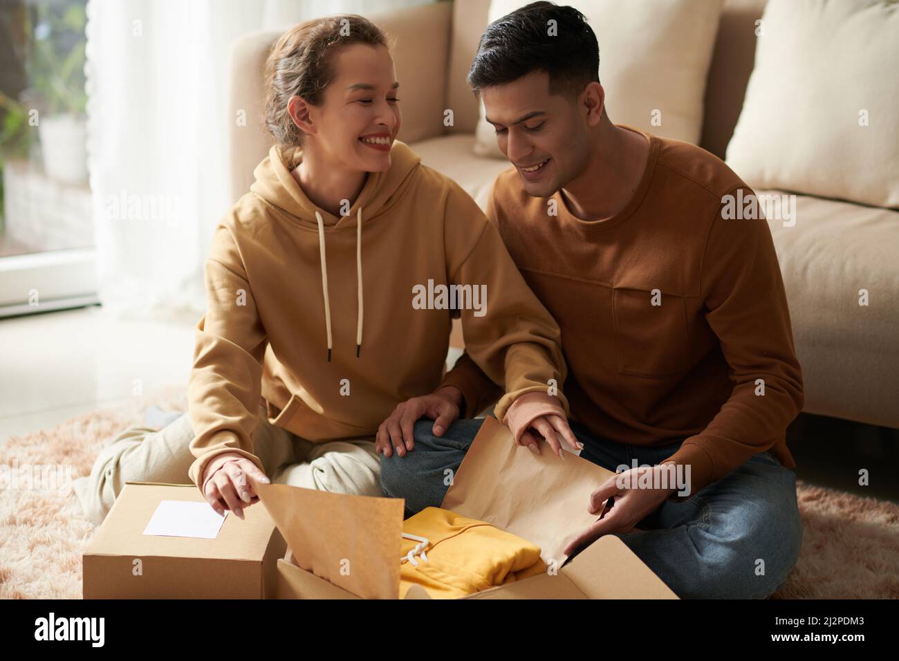 Joyfu young couple opening boxes with clothes they ordered for each ...