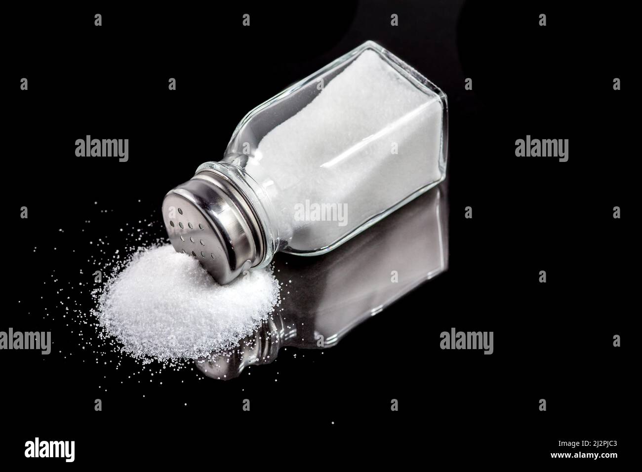 Salt shaker with spilled salt on a black background Stock Photo - Alamy