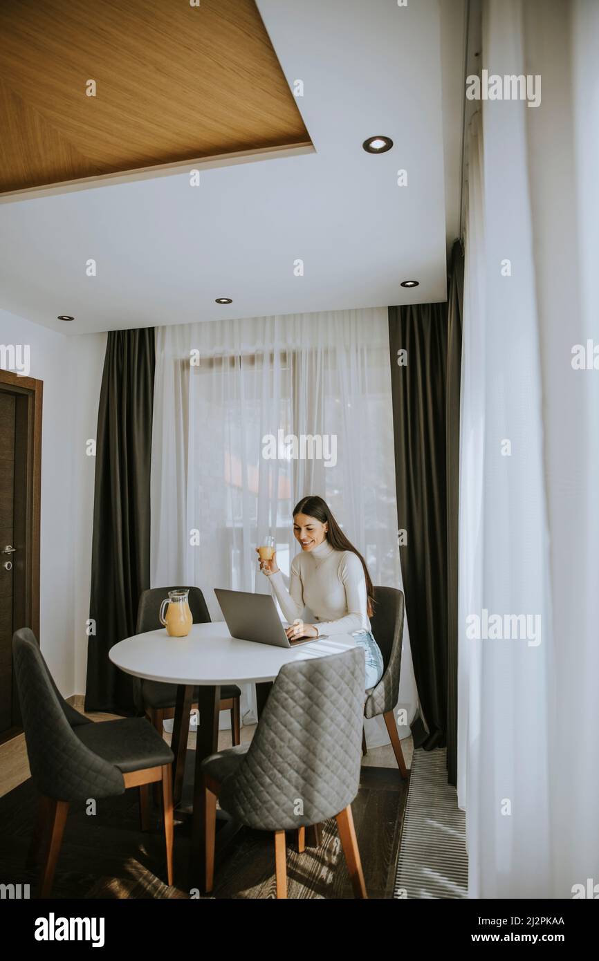 Young woman using a laptop computer and drinking healthy orange juice ...