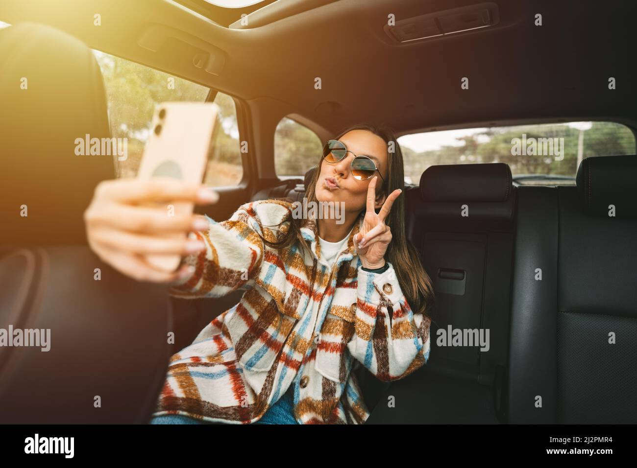 Stylish young woman sitting on back seat in the car and making selfie ...