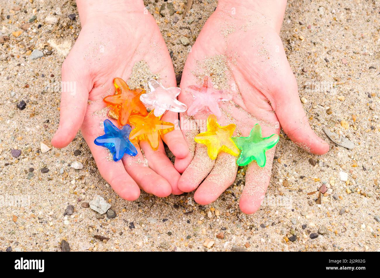 Multicolored decorative stars in hands on the background of beach sand ...