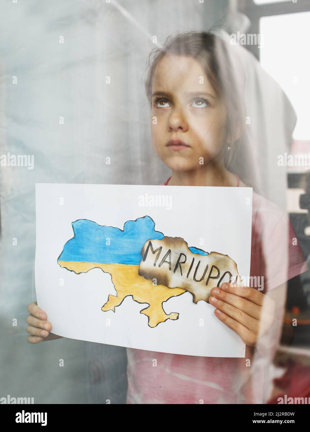 a little Ukrainian girl with sad eyes is standing behind the glass ...