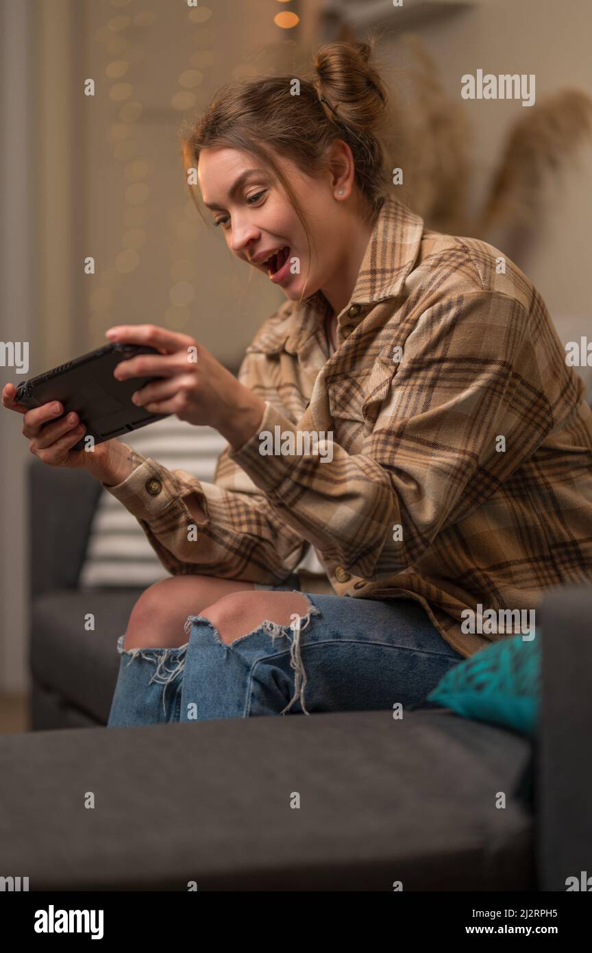 A cute girl gamer in youth clothes has fun playing mobile games on a ...