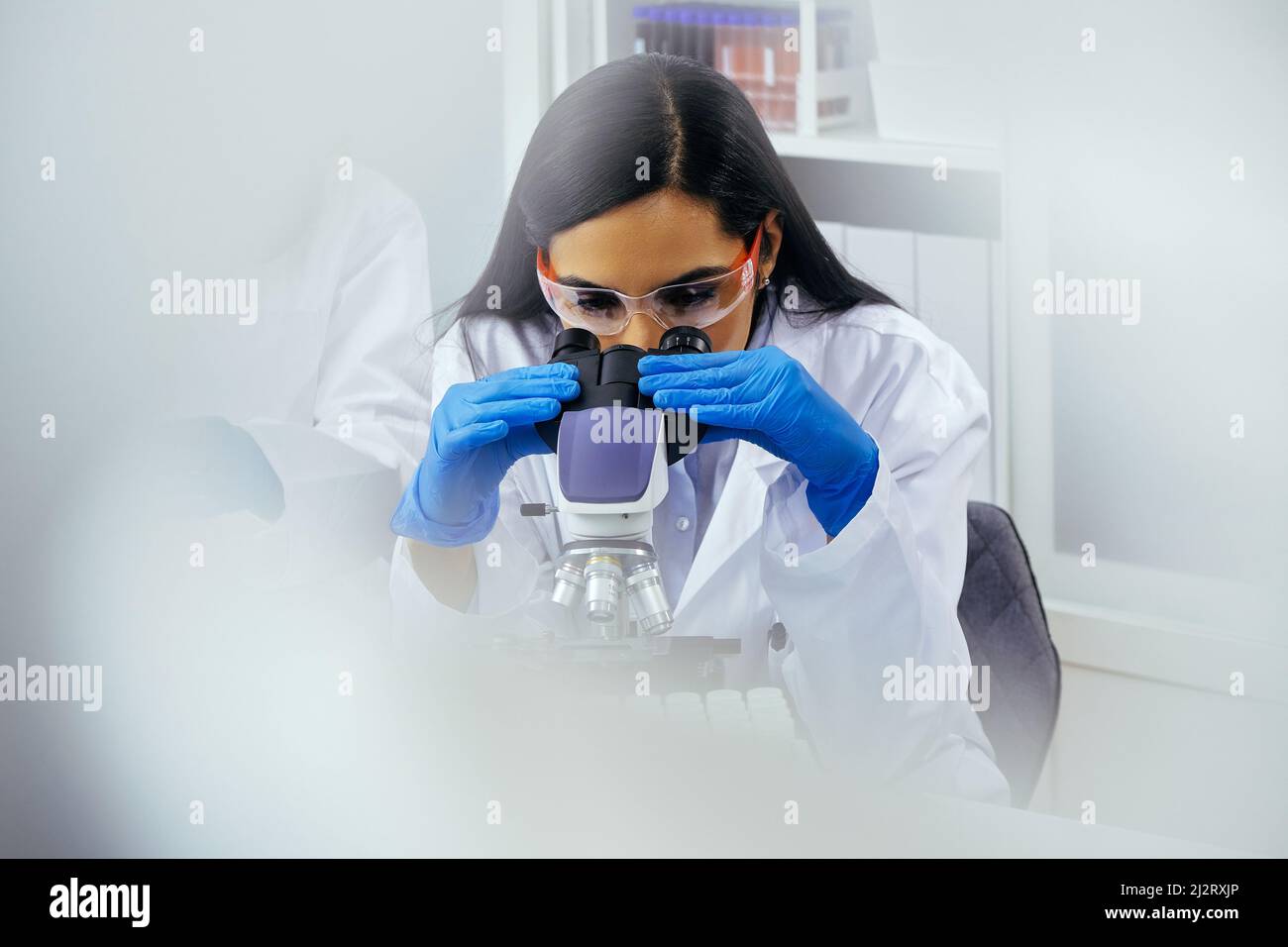 Beautiful young scientist or laboratory assistant using microscope in ...