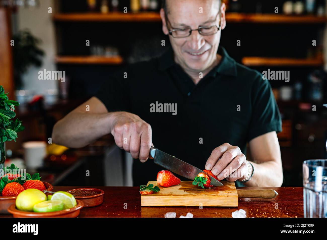 Older waiter cutting strawberries to prepare a cocktail. Senior ...
