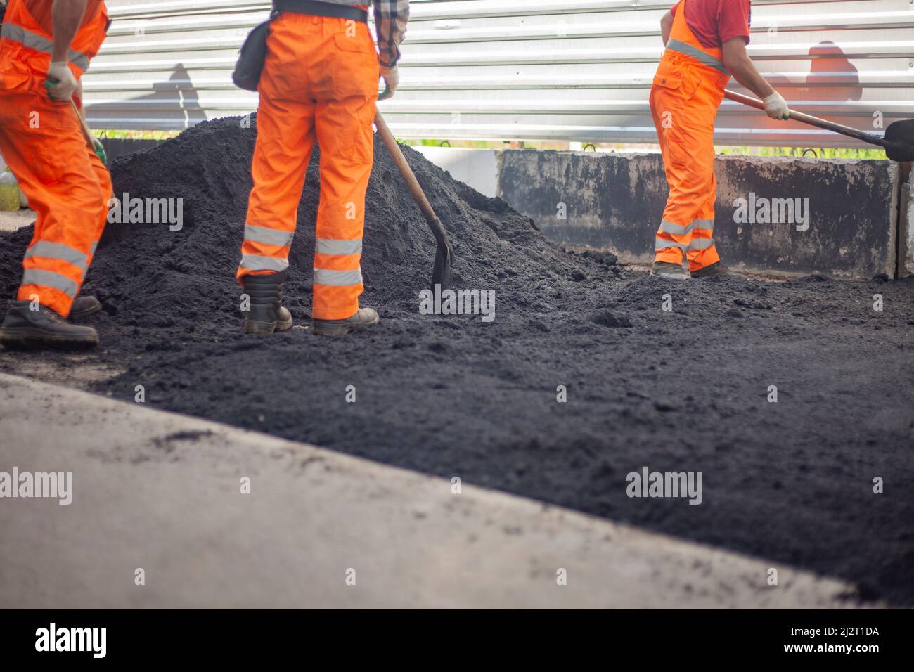 A bunch of asphalt. Workers repair the road. People in orange clothes ...