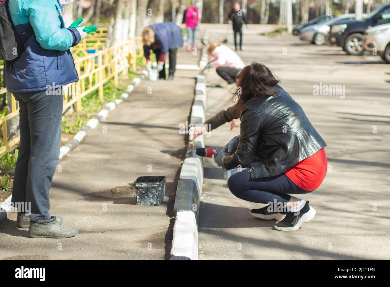 People paint the curb. A girl with a brush in a leather jacket and a ...