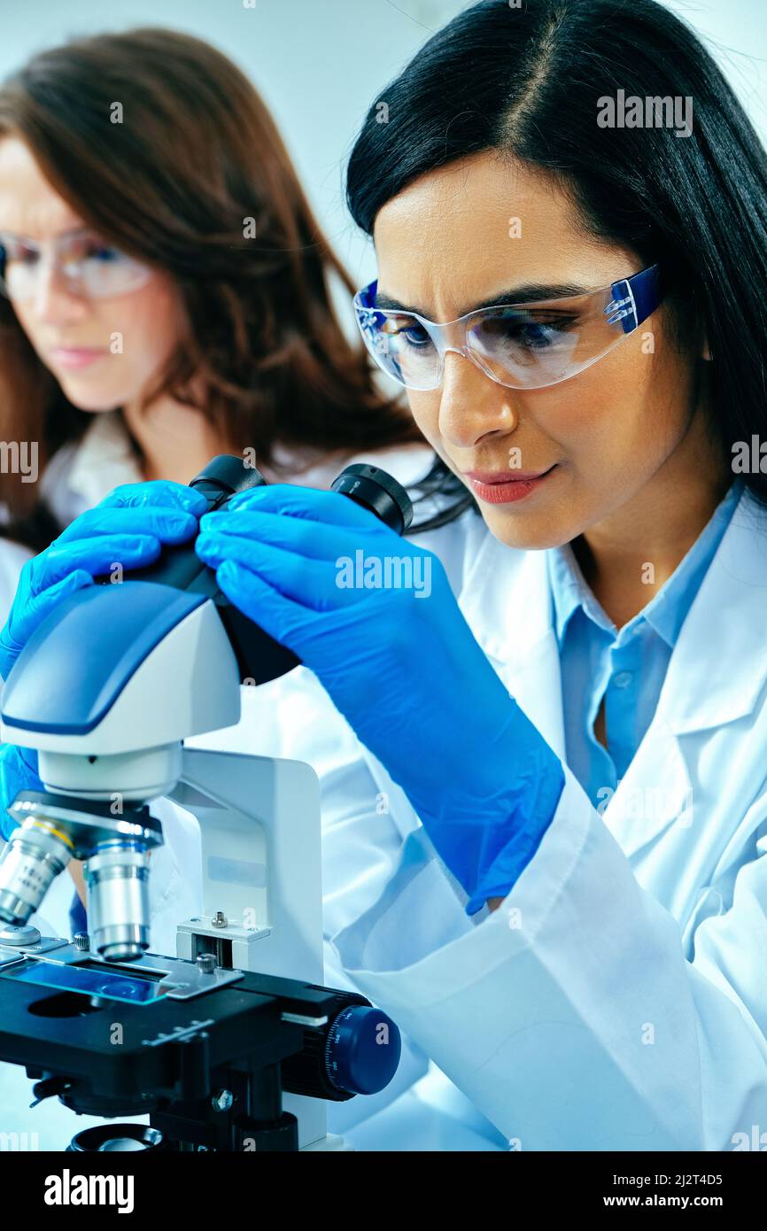 Young female scientist using microscope while her colleague working in ...
