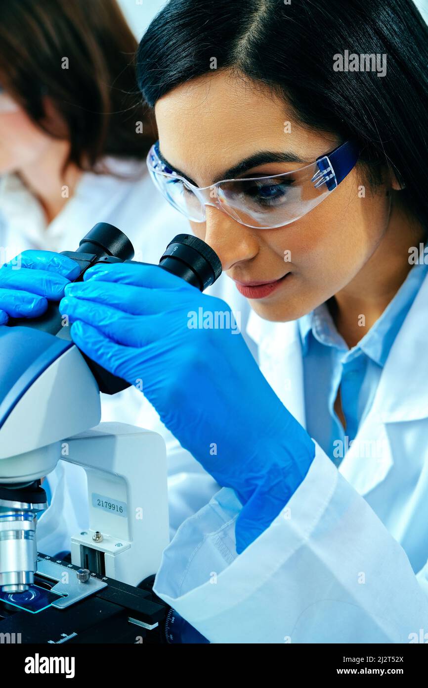 Young female scientist using microscope while her colleague working in ...