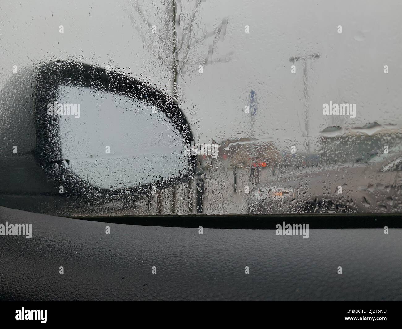 Raindrops and blurred exterior seen from inside a car on a grey rainy ...