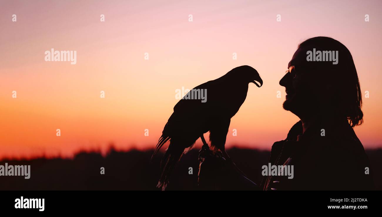 Banner Silhouette of man and wild bird over sunset sky looking on each ...
