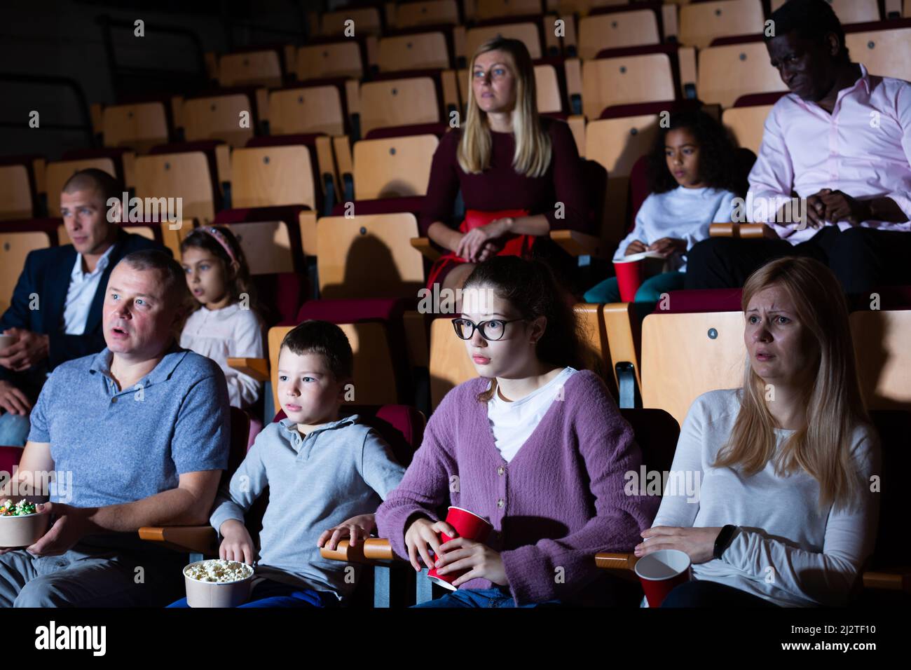 Scared and shocked adults and children watching movie in cinema Stock ...