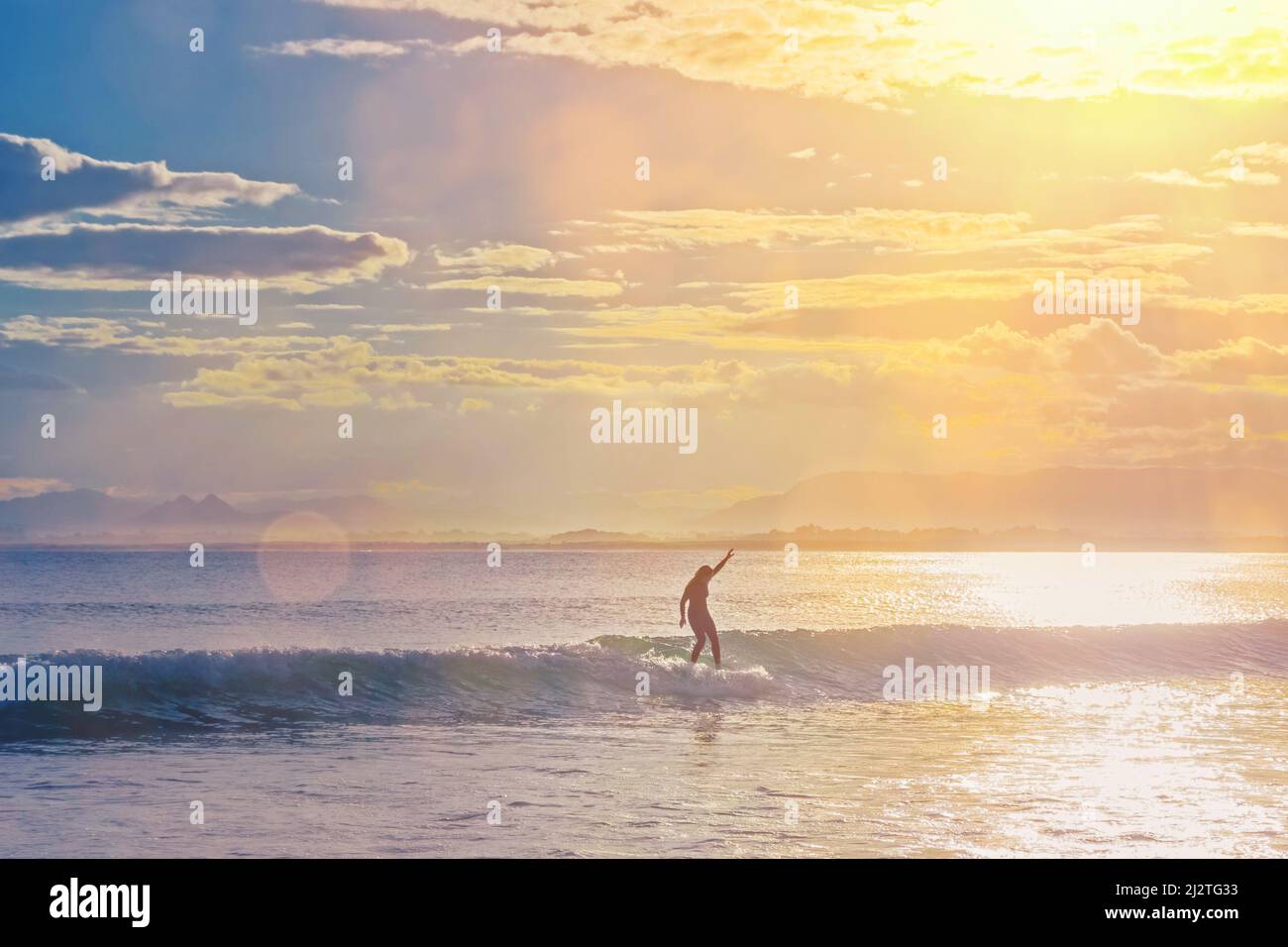 Silhouette of a surfer riding a small wave on a hot summer’s day in ...