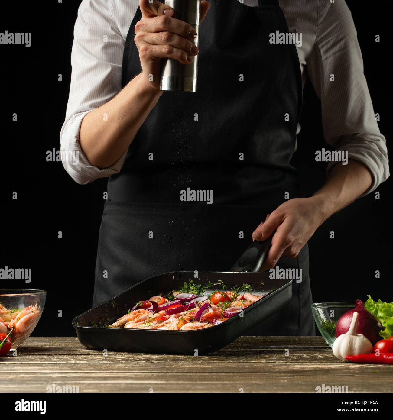Professional chef salting shrimps with vegetables on the grill pan ...