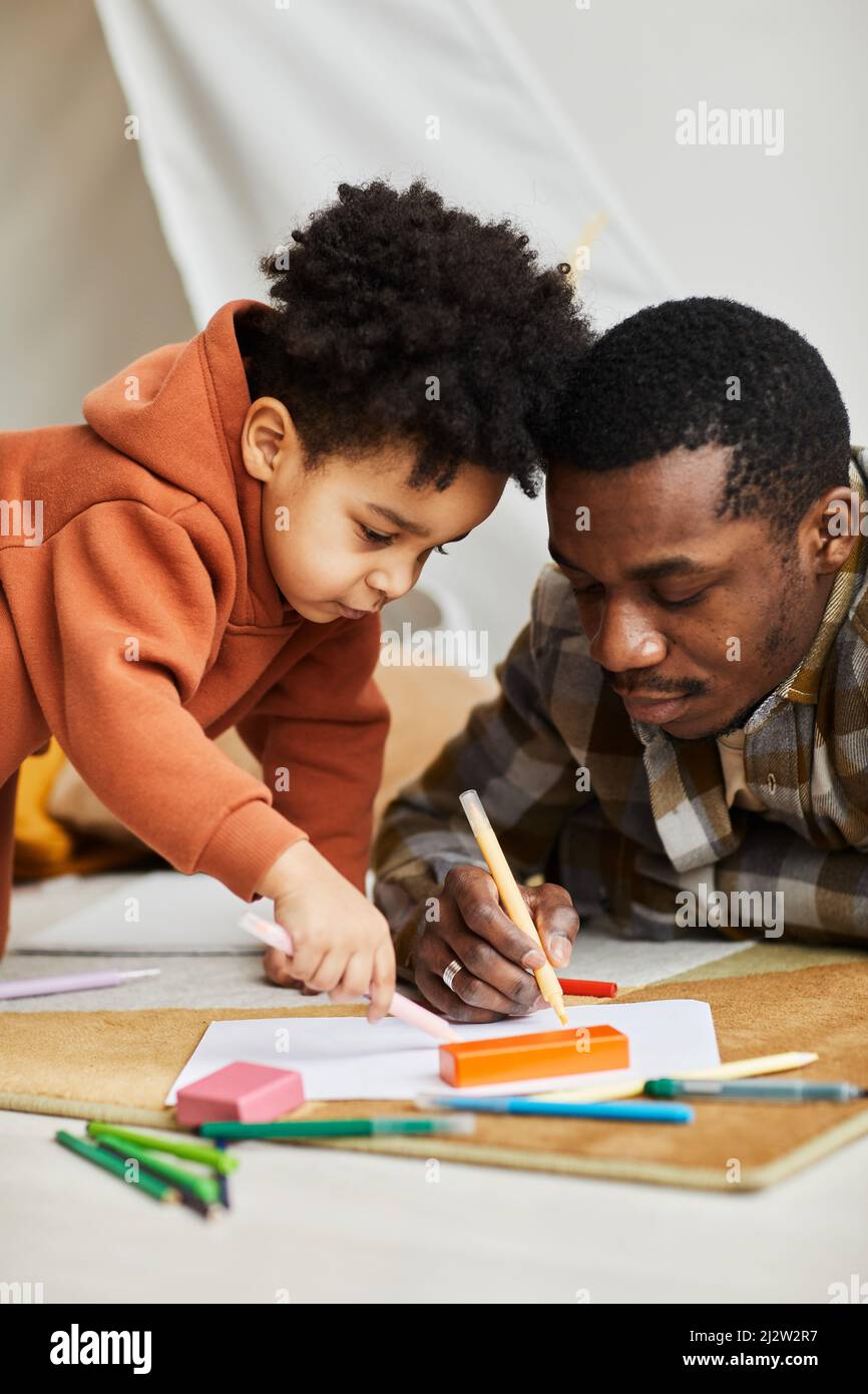 Vertical portrait of loving father and son drawing together on floor in ...