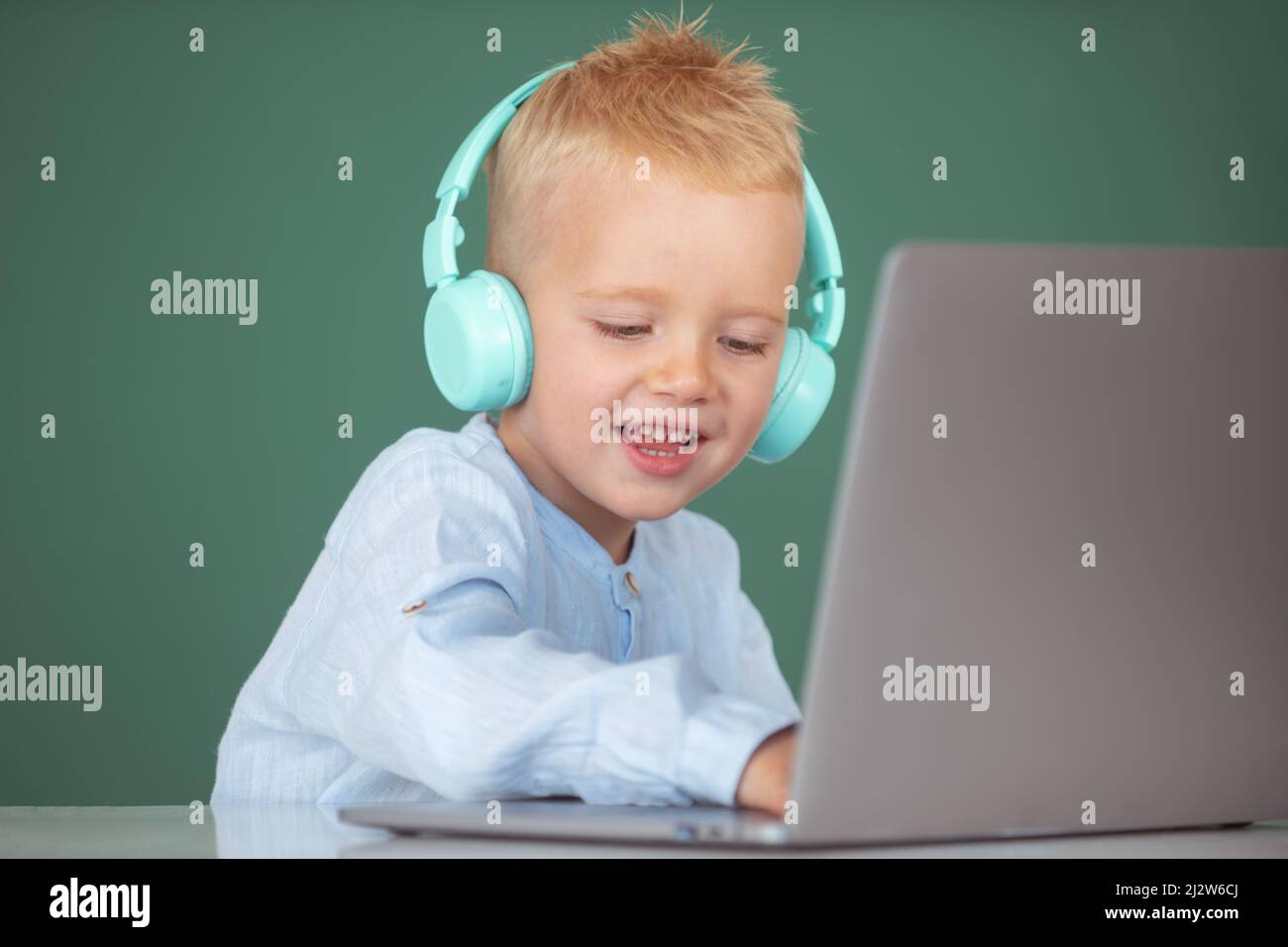 Clever school boy, cute pupil wears headphones writing on laptop ...