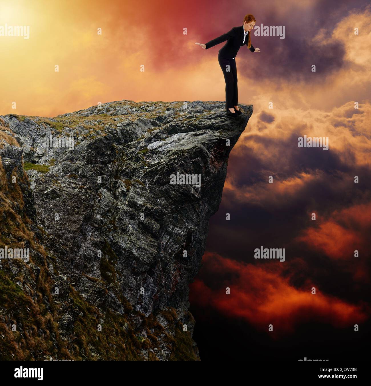 Businesswoman on the edge of a high cliff looking down into the abyss ...