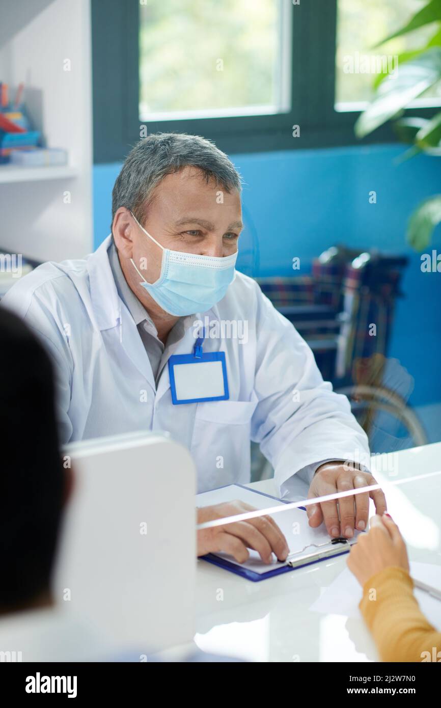 Positive general practitioner consulting patient at client reception ...