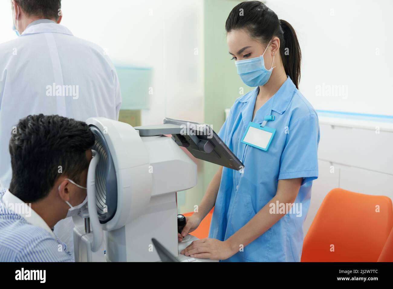 Serious young medical nurse looking at screen of refractometer machine ...