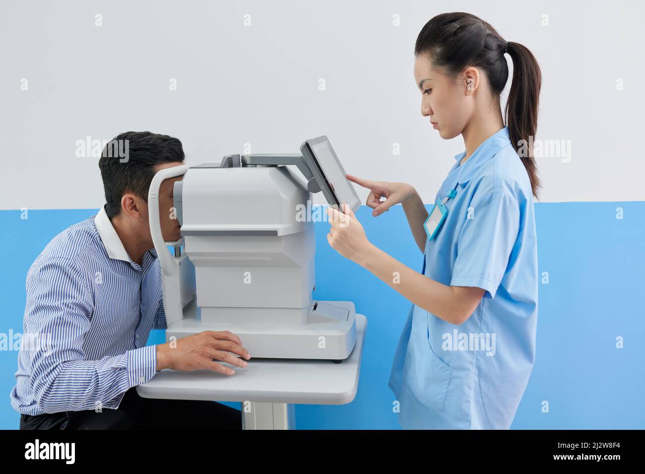 Young female doctor setting refractometer machine to check eyes of ...