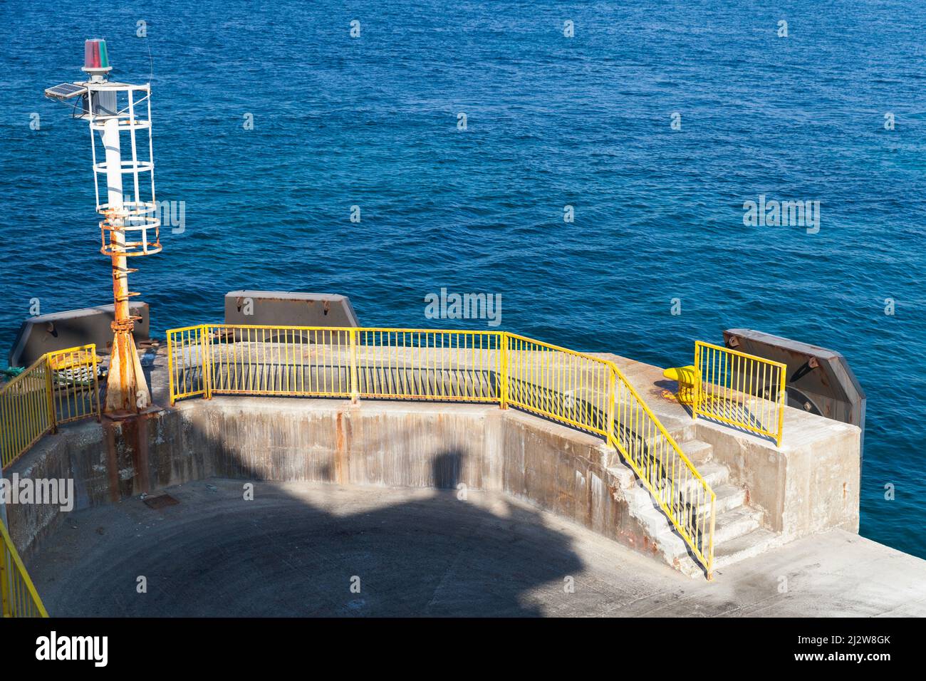 Concrete pier with yellow railings and lighthouse pole, port navigation ...