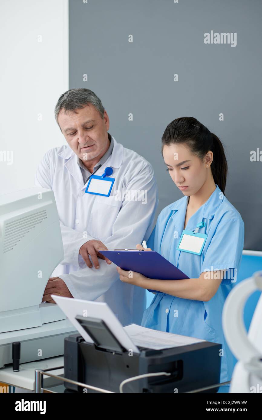 Ophthalmologist asking nurse to take notes in medical form when he is ...