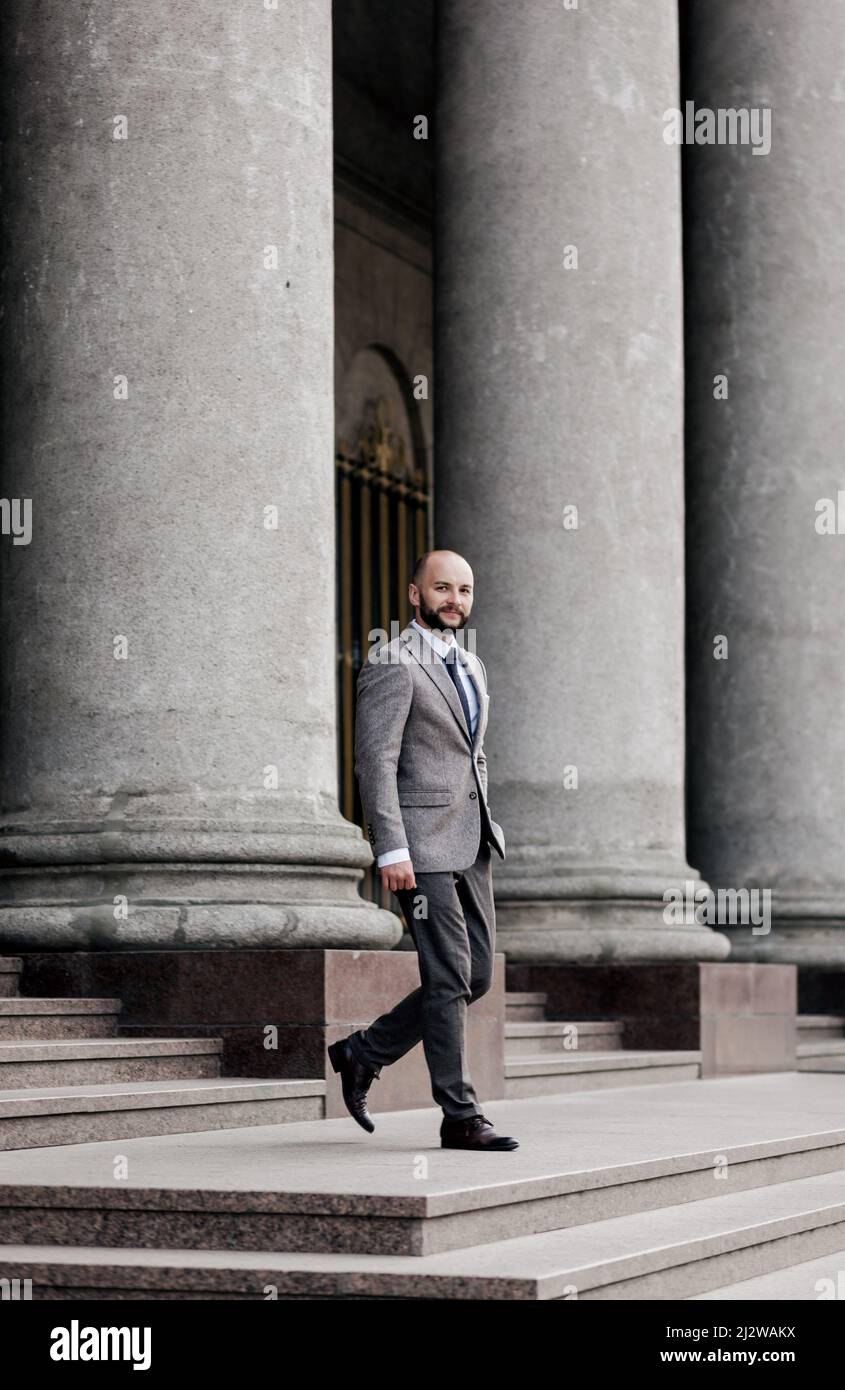 Stylish young bearded man walking on steps. He is in a suit, pensive ...