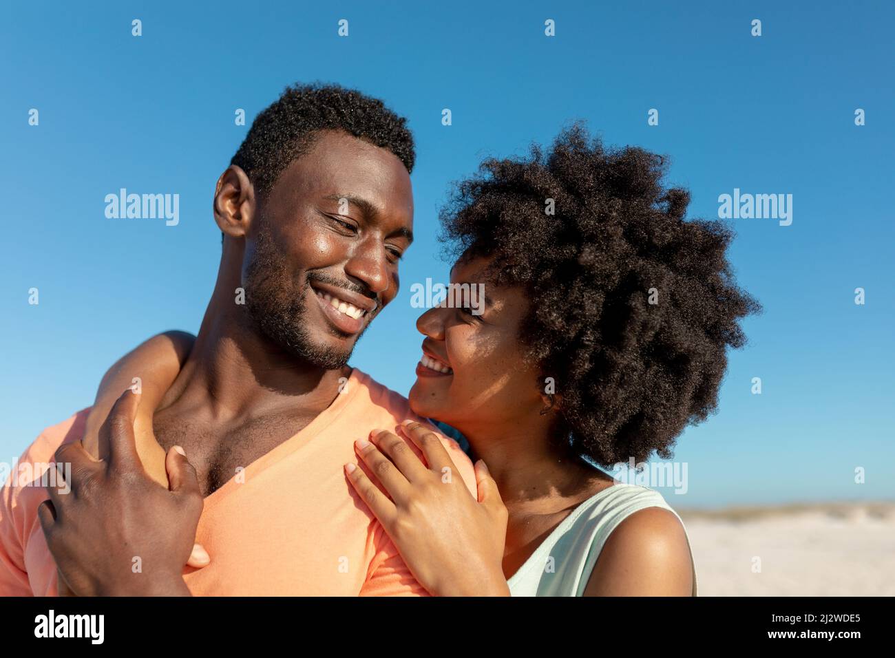 Romantic african american couple looking at each other against blue sky ...