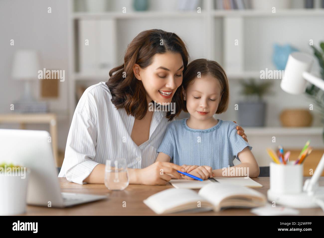 Happy child and adult are sitting at desk. Girl doing homework or ...