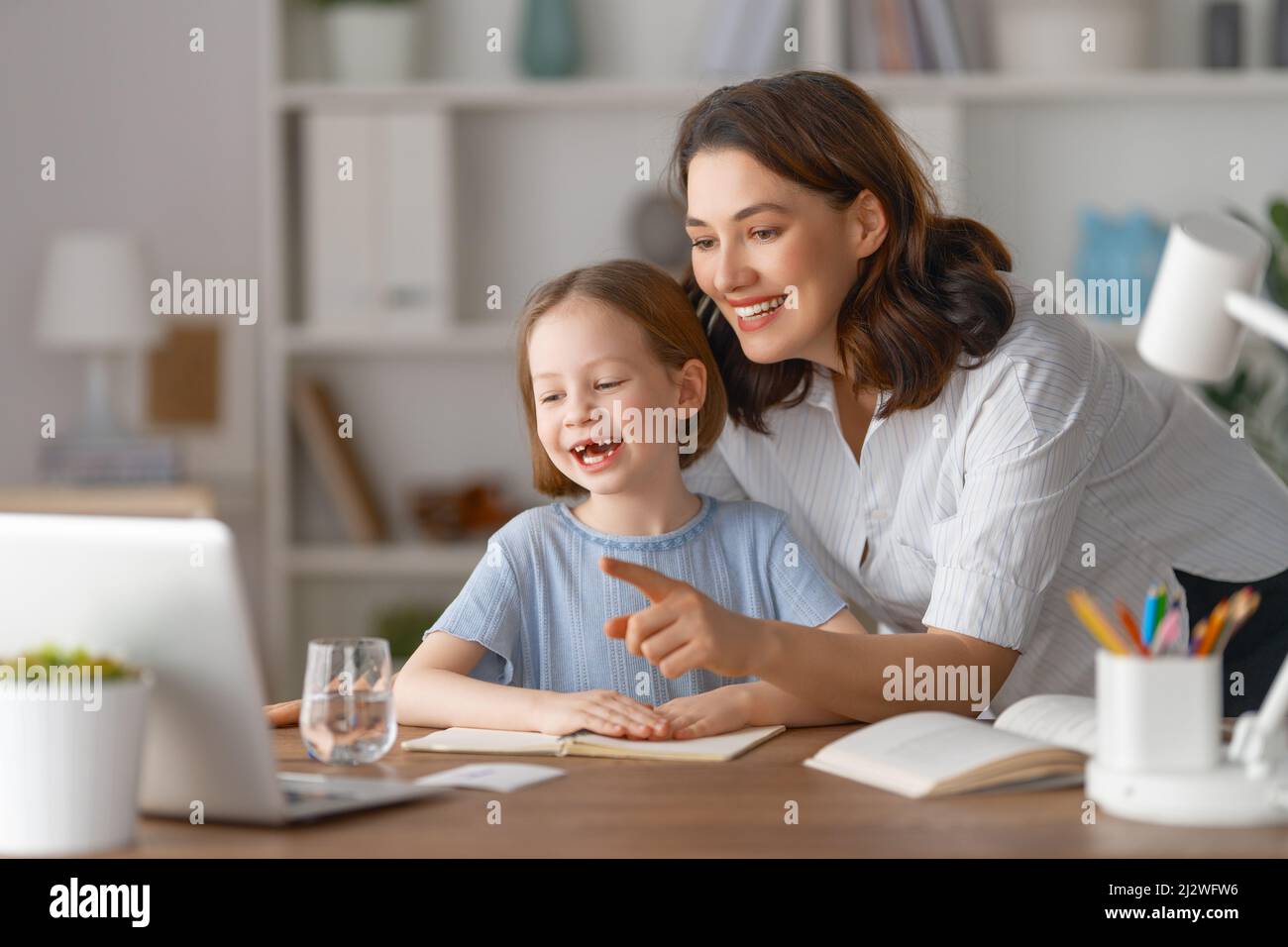 Happy child and adult are sitting at desk. Girl doing homework or ...