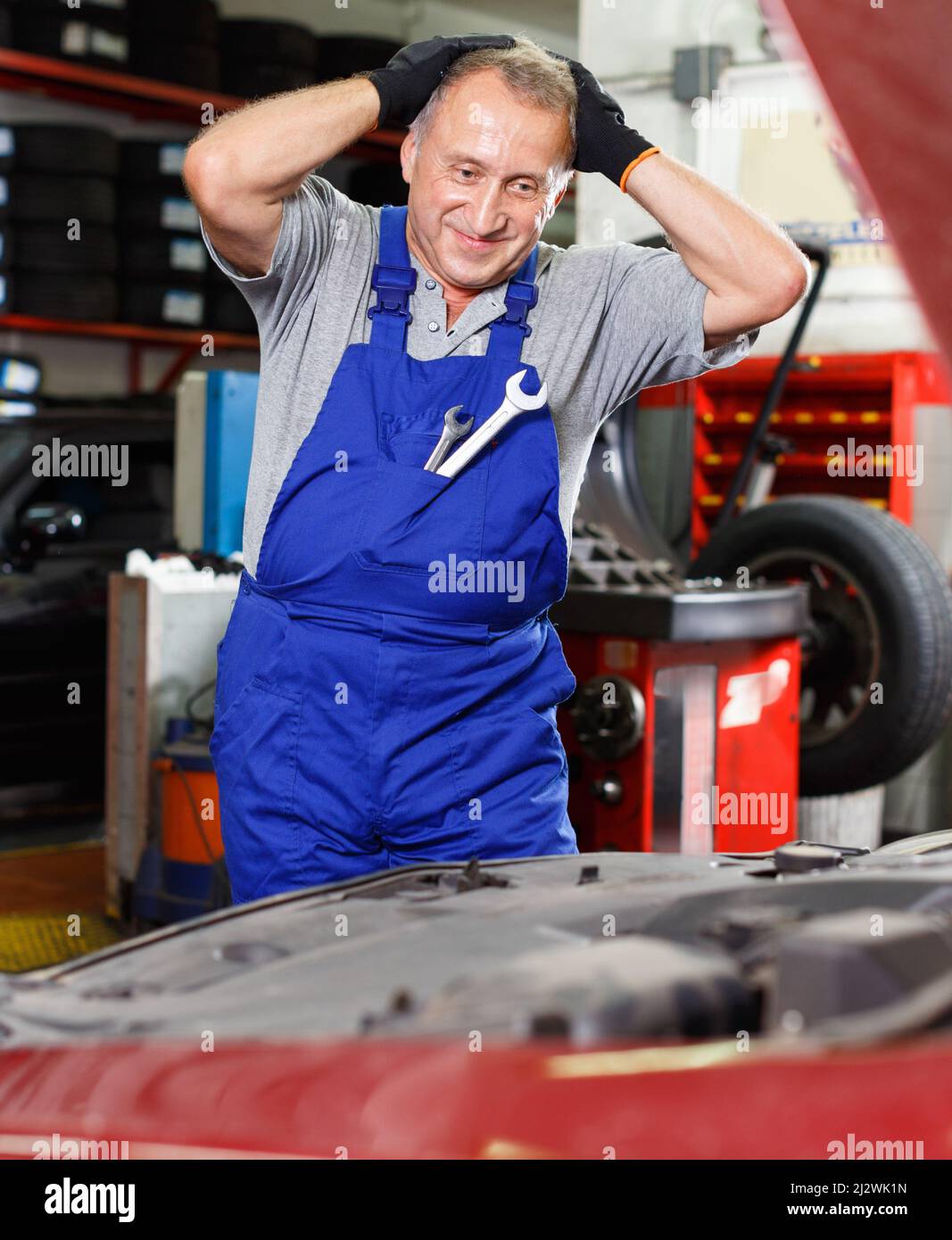 Puzzled male mechanic inspecting broken car and determining scope of ...