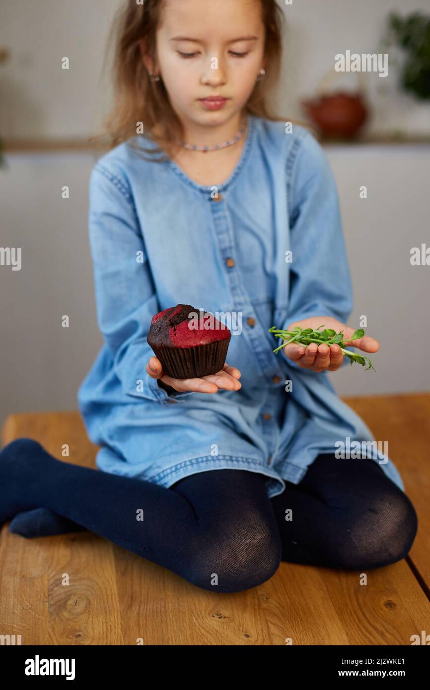 Little girl comparing food, choosing microgreen against sweet cake ...
