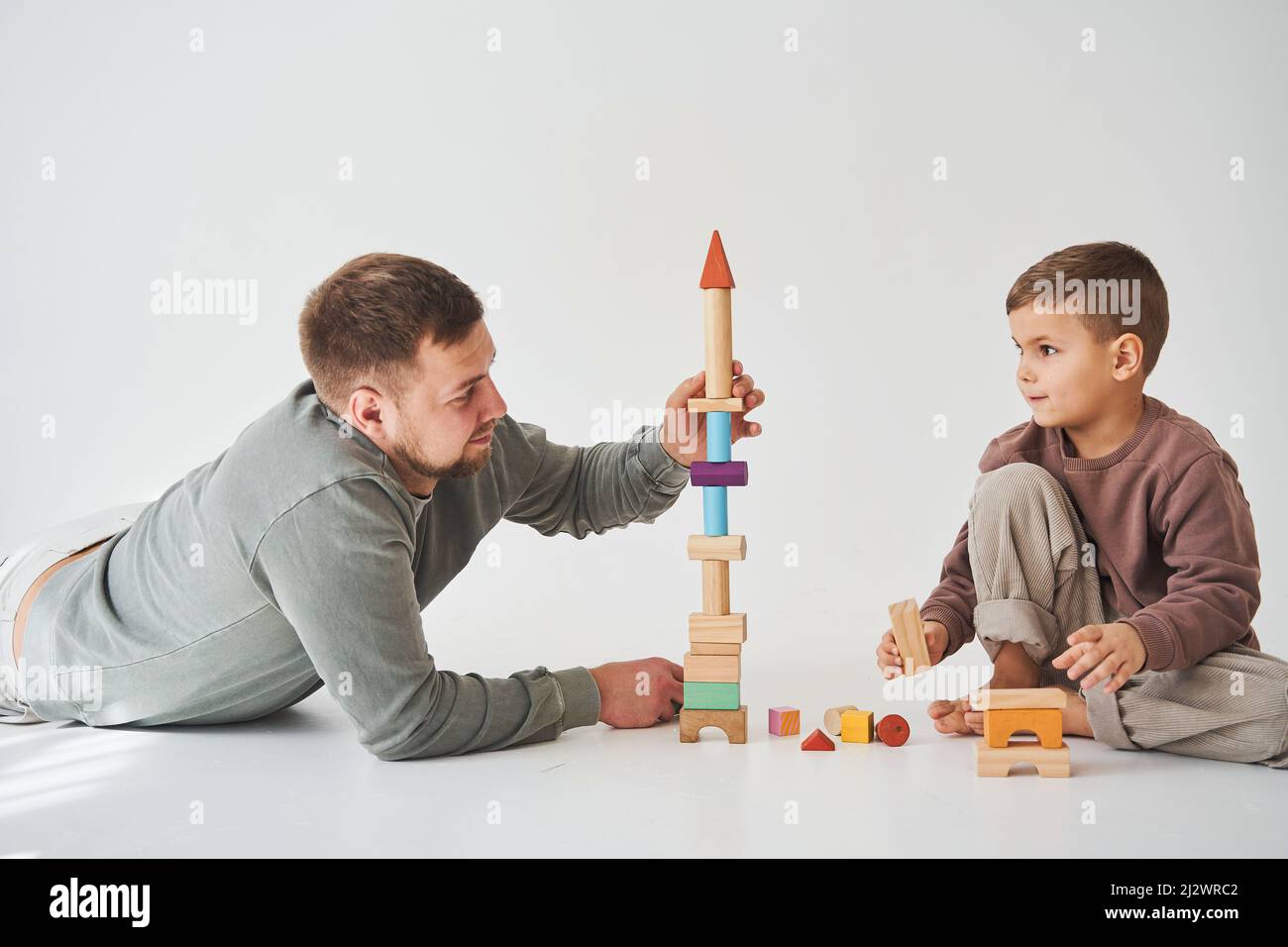 Caring dad helps his son to play on the floor on white background ...