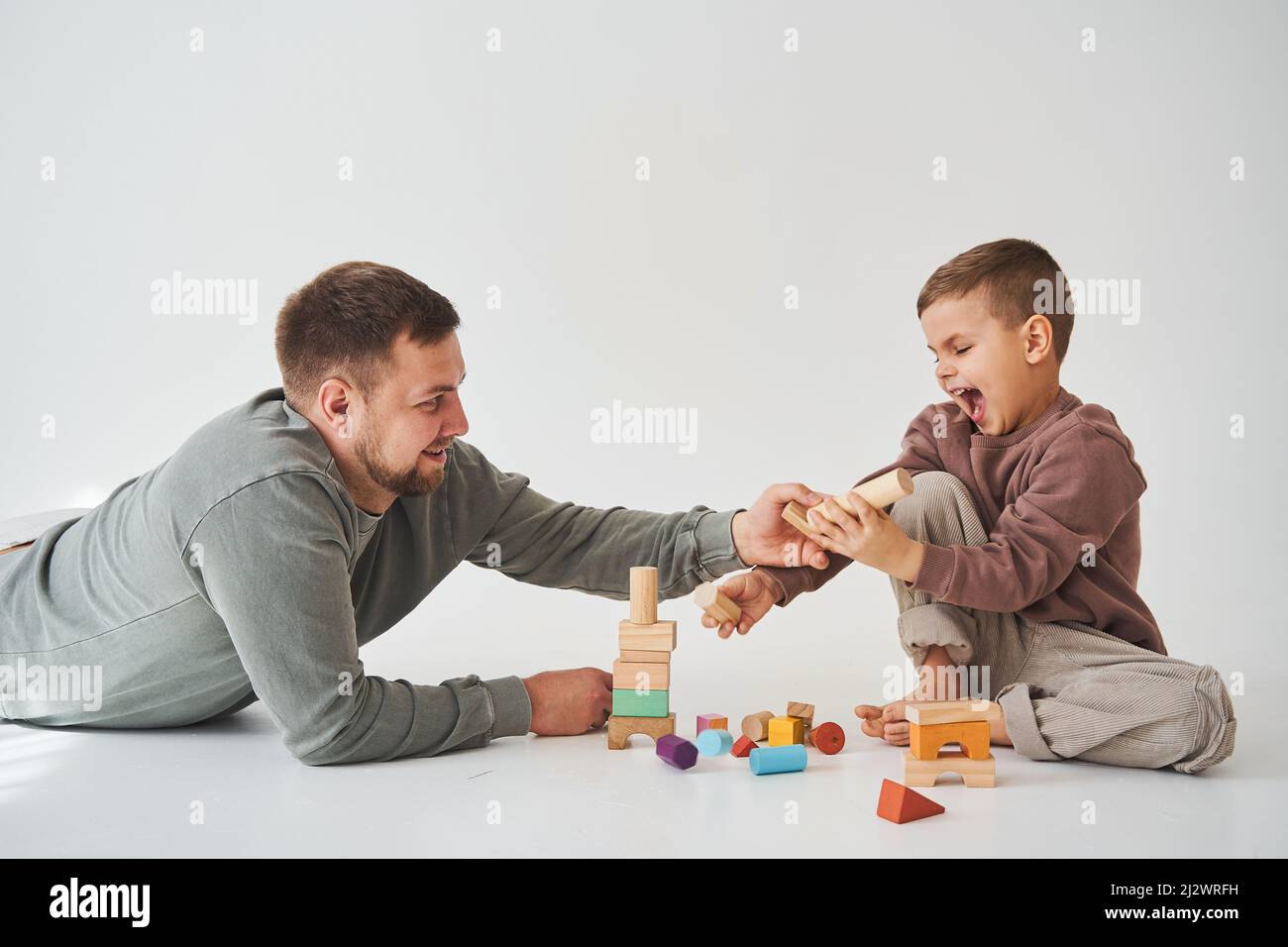 Dad and son smiling, having fun and playing colored bricks toy on white ...