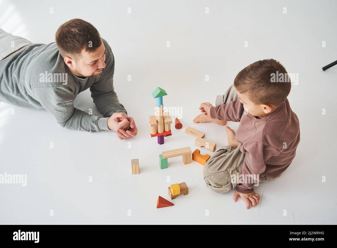 Caring dad helps his son to play on the floor on white background ...