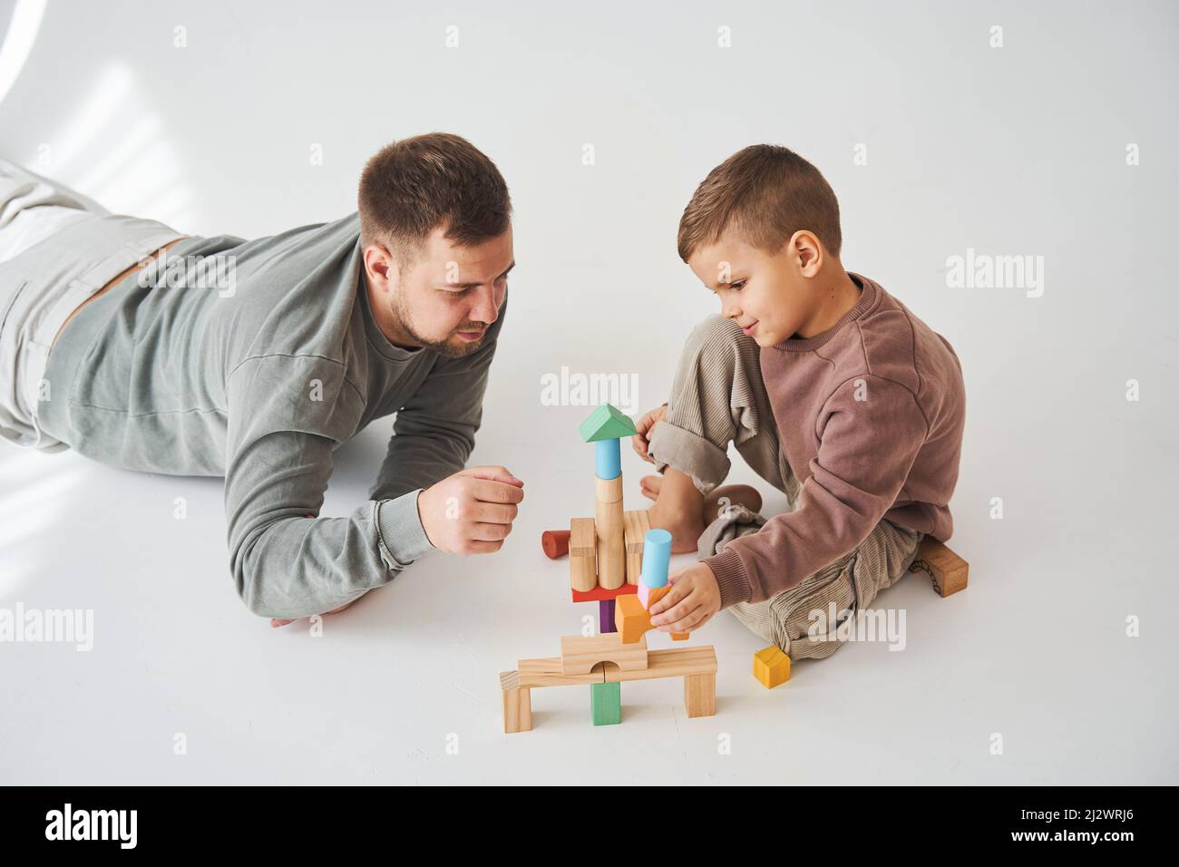 Caring dad helps his son to play on the floor on white background ...